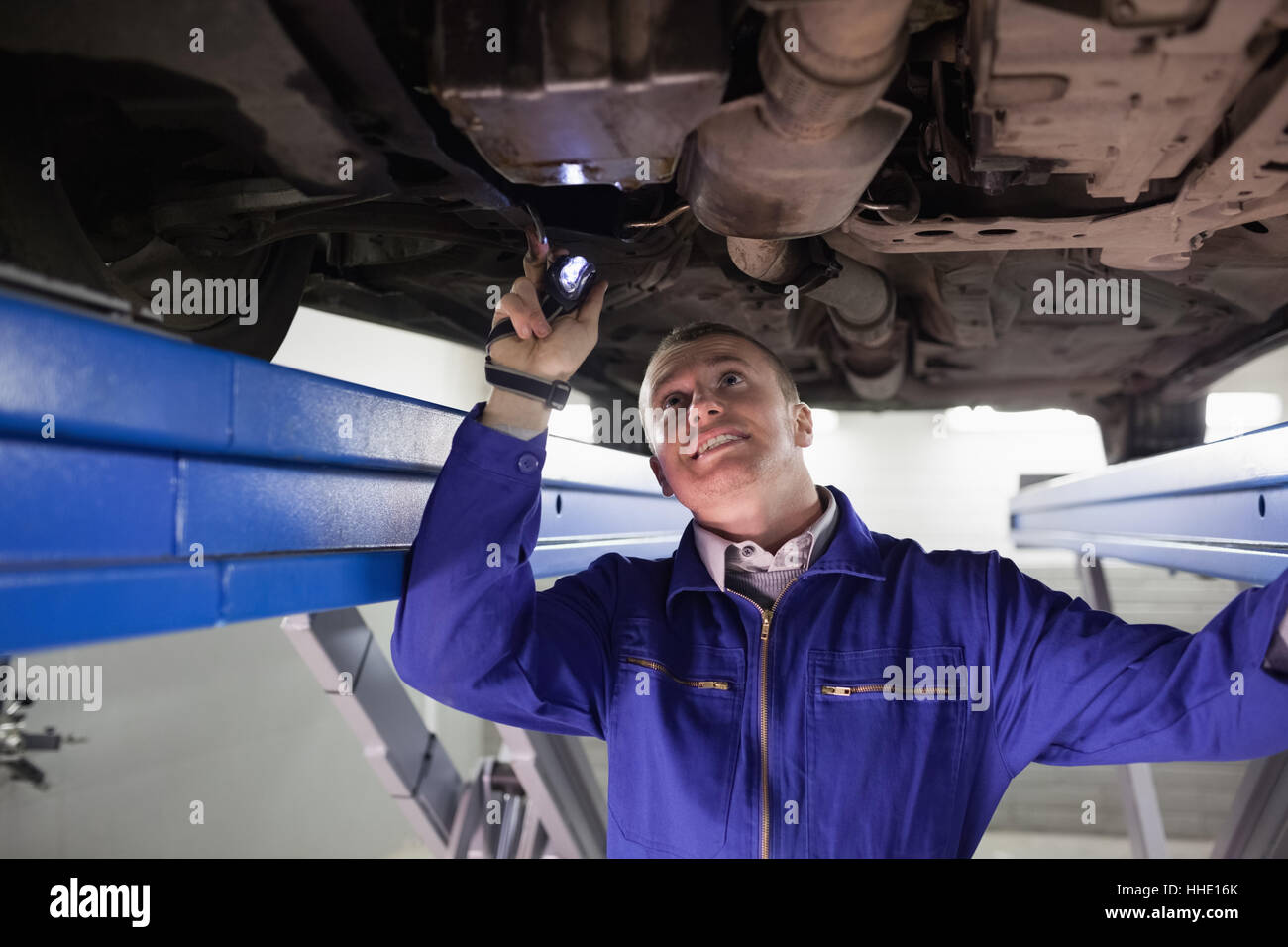 Smiling mechanic illuminating a car with a flashlight in a garage Stock ...