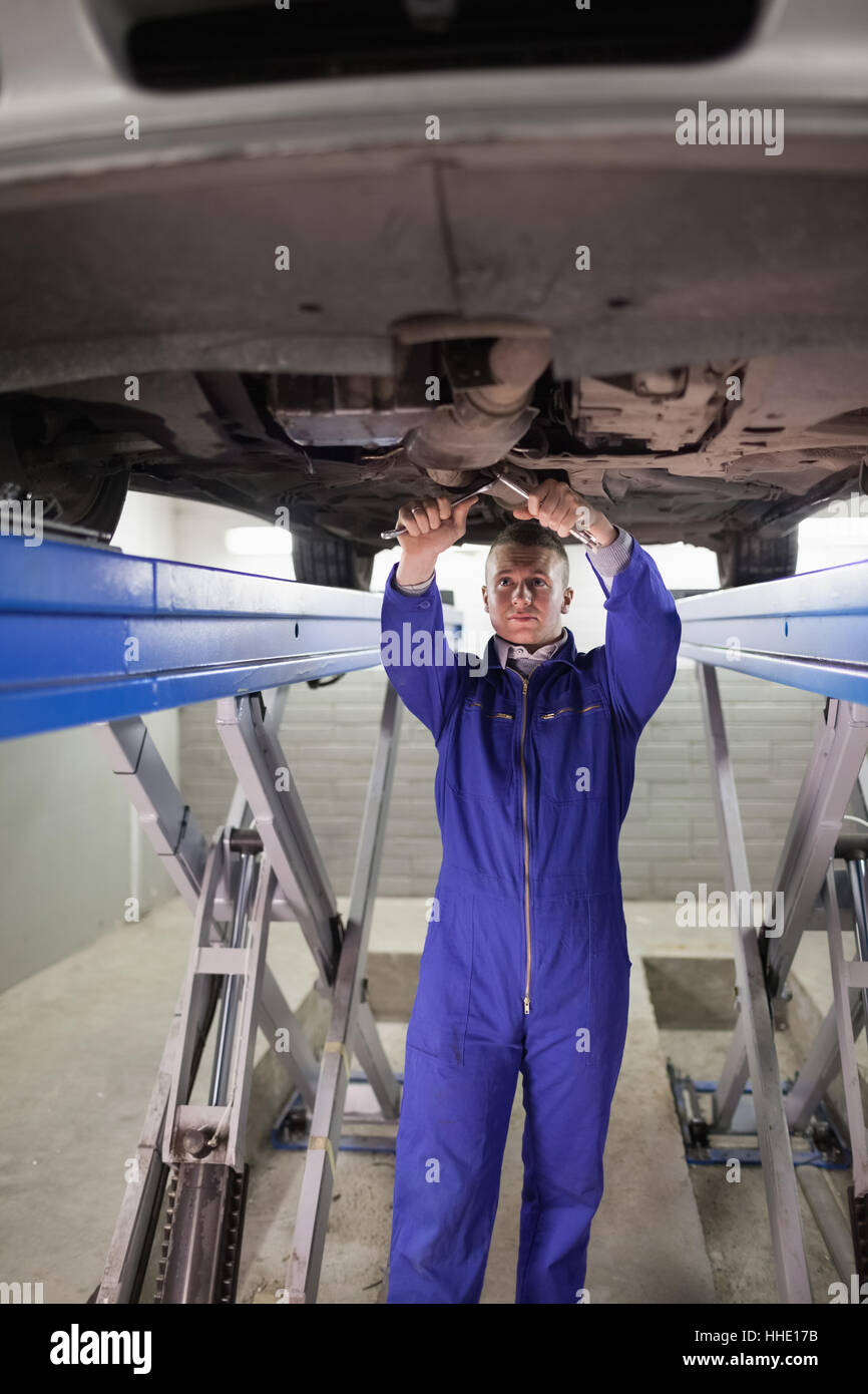 Mechanic standing while repairing the below of a car in a garage Stock ...