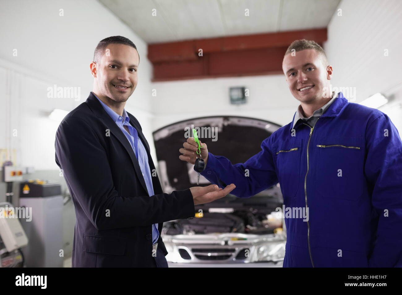 Mechanic smiling while giving car key to a man in a garage Stock Photo ...
