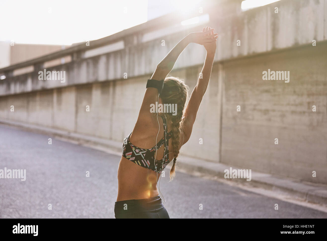 Fit female runner in sports bra stretching arms overhead on urban ...