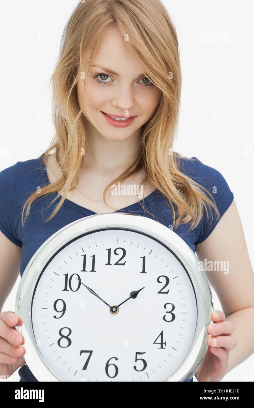 Woman holding a clock while looking at camera against a white ...