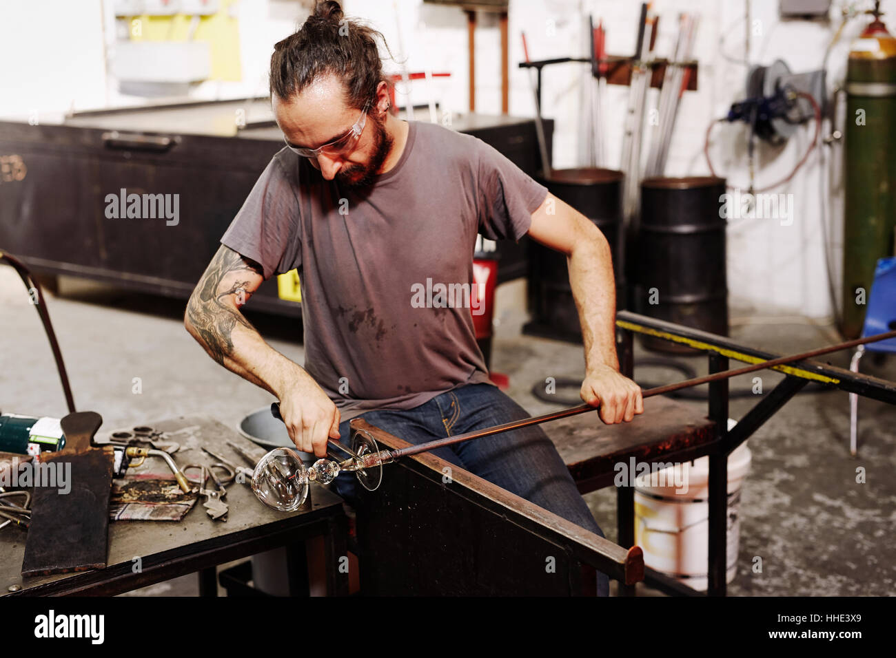 A glassblower working on a shaped piece of glass and using a chisel to ...