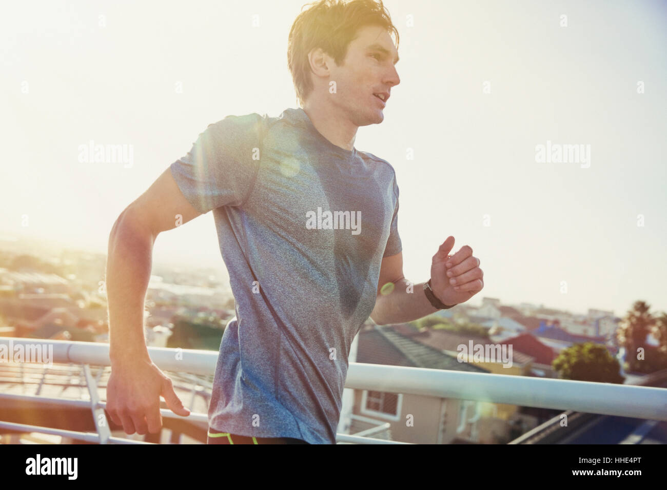 Sweaty male runner running on sunny urban footbridge at sunrise Stock ...