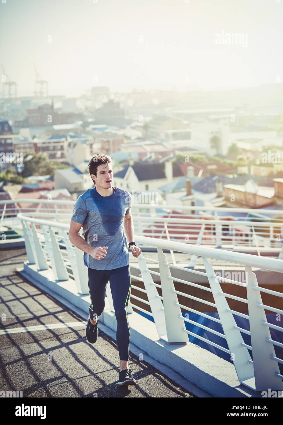 Sweaty male runner running on sunny urban footbridge at sunrise Stock ...