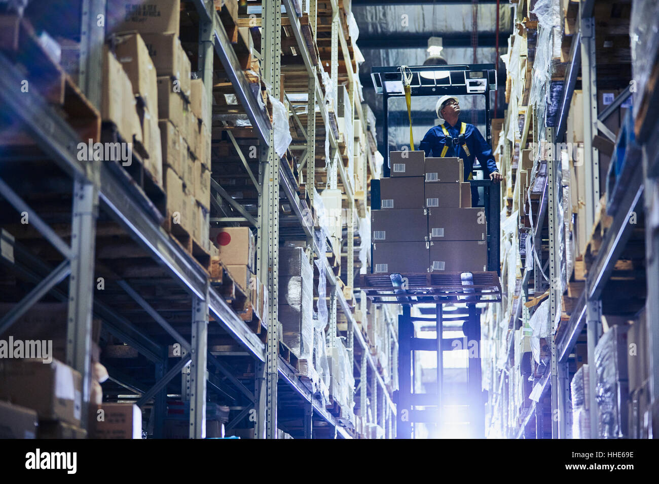 Worker operating forklift stacking cardboard boxes on distribution ...