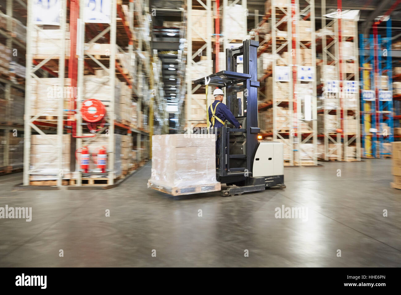 Worker operating forklift moving pallet of boxes in distribution ...