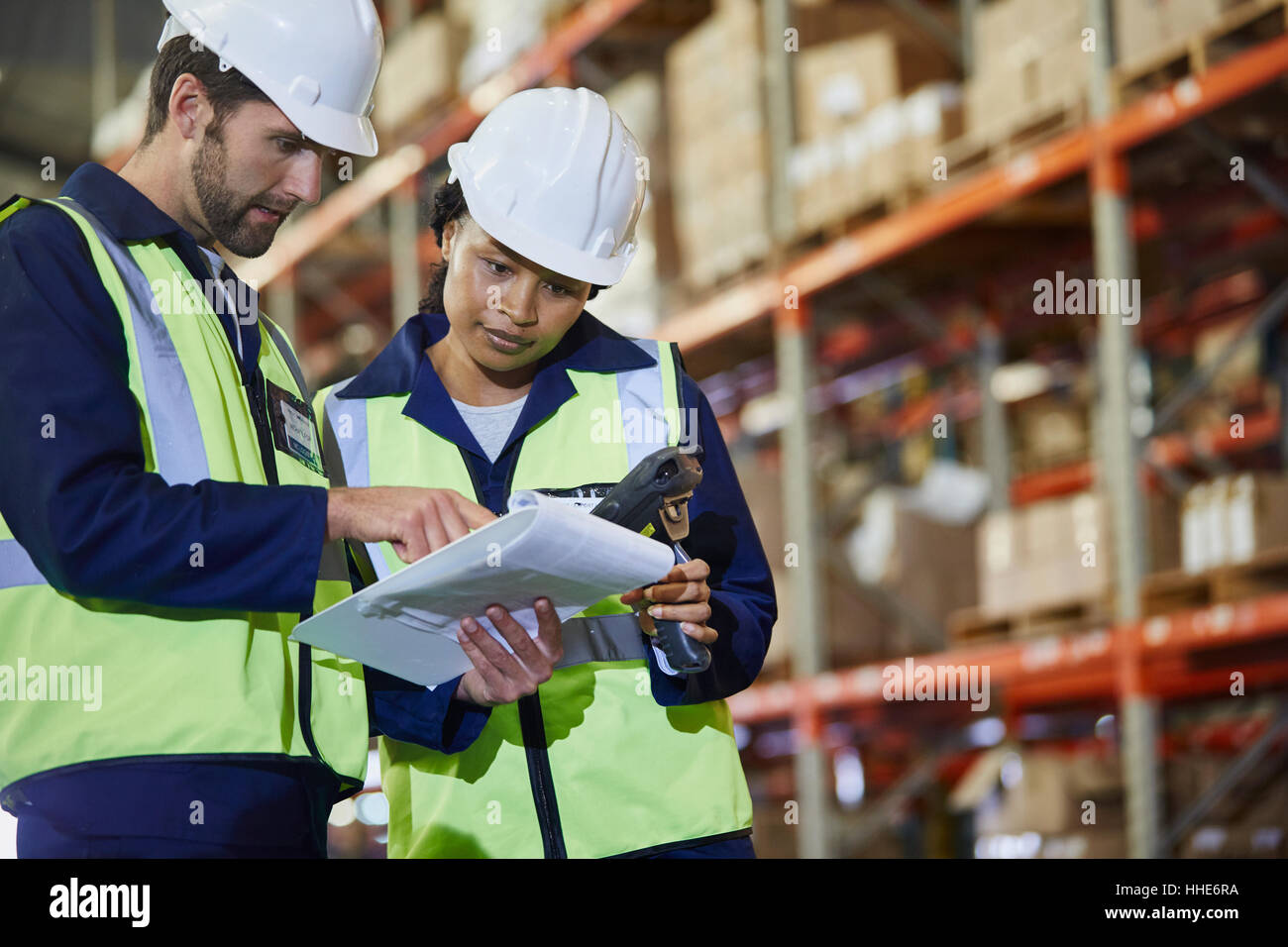 Workers with scanner and clipboard talking in distribution warehouse ...
