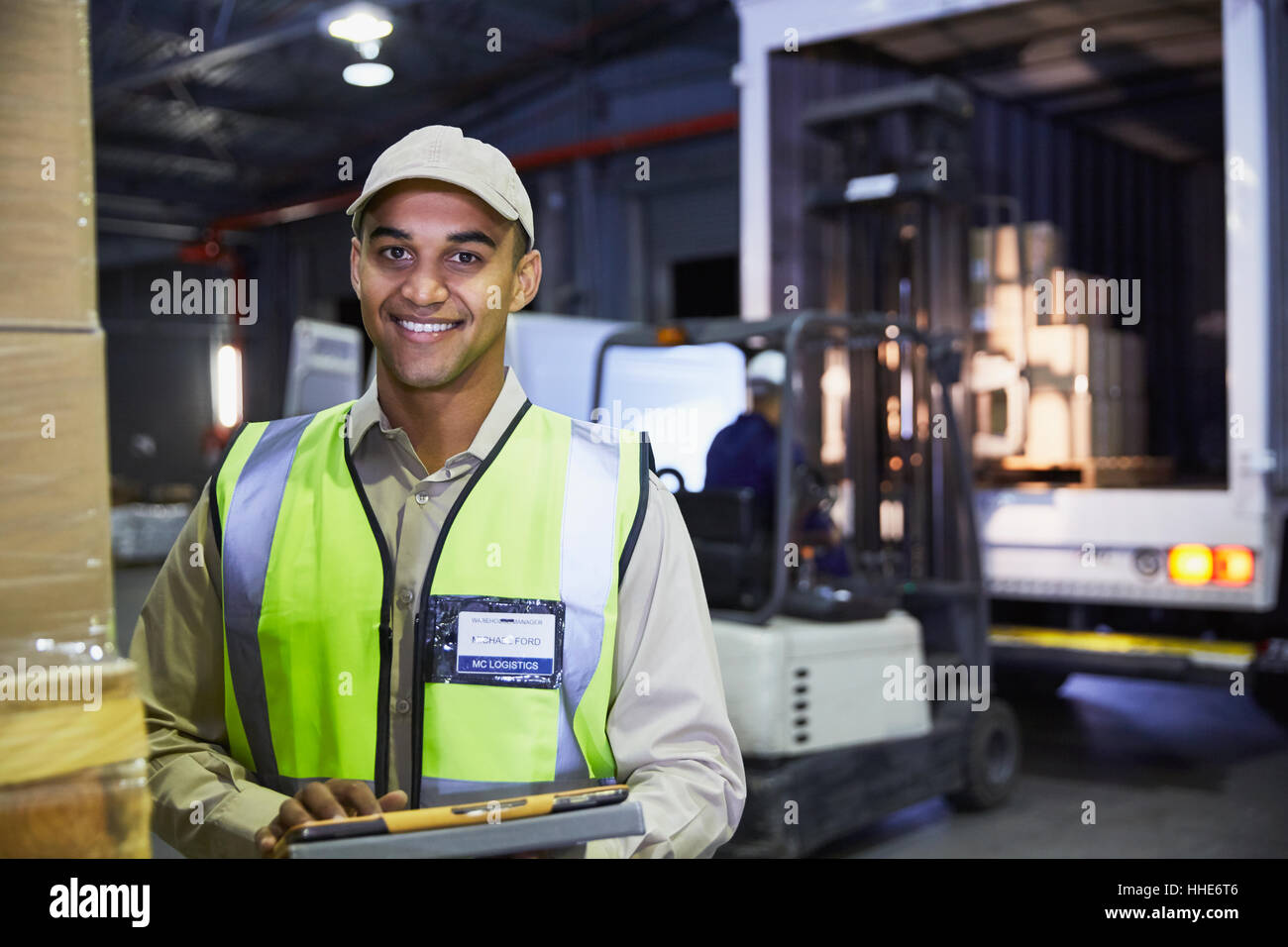 Portrait smiling worker in front of forklift and truck at distribution ...