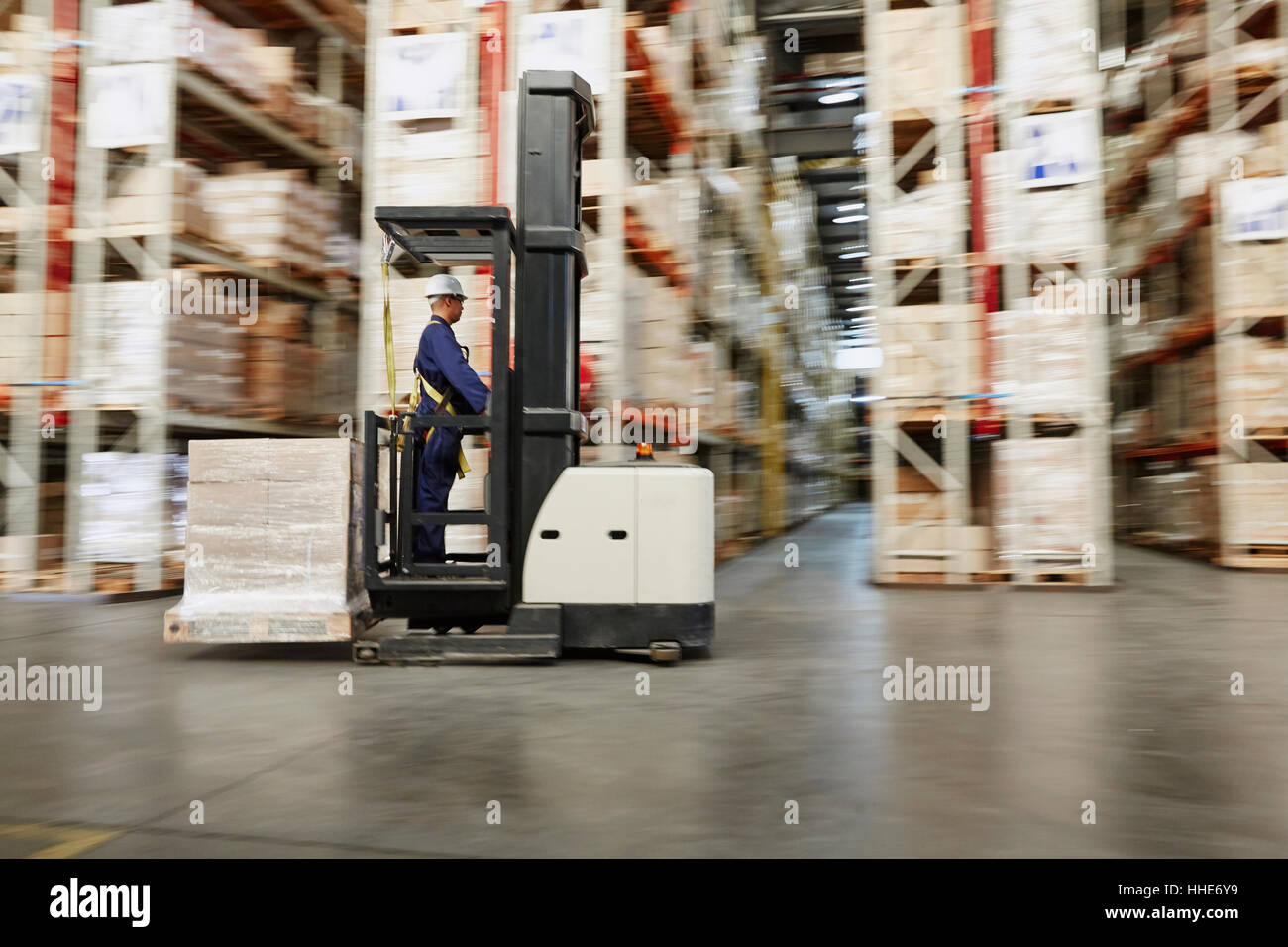 Worker operating forklift moving pallet of boxes in distribution ...