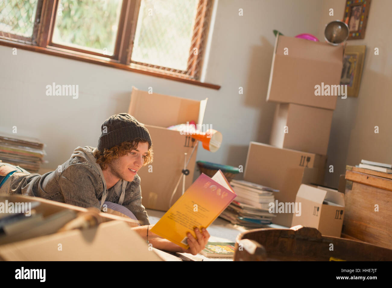 Young man reading book surrounded by moving boxes in apartment Stock ...