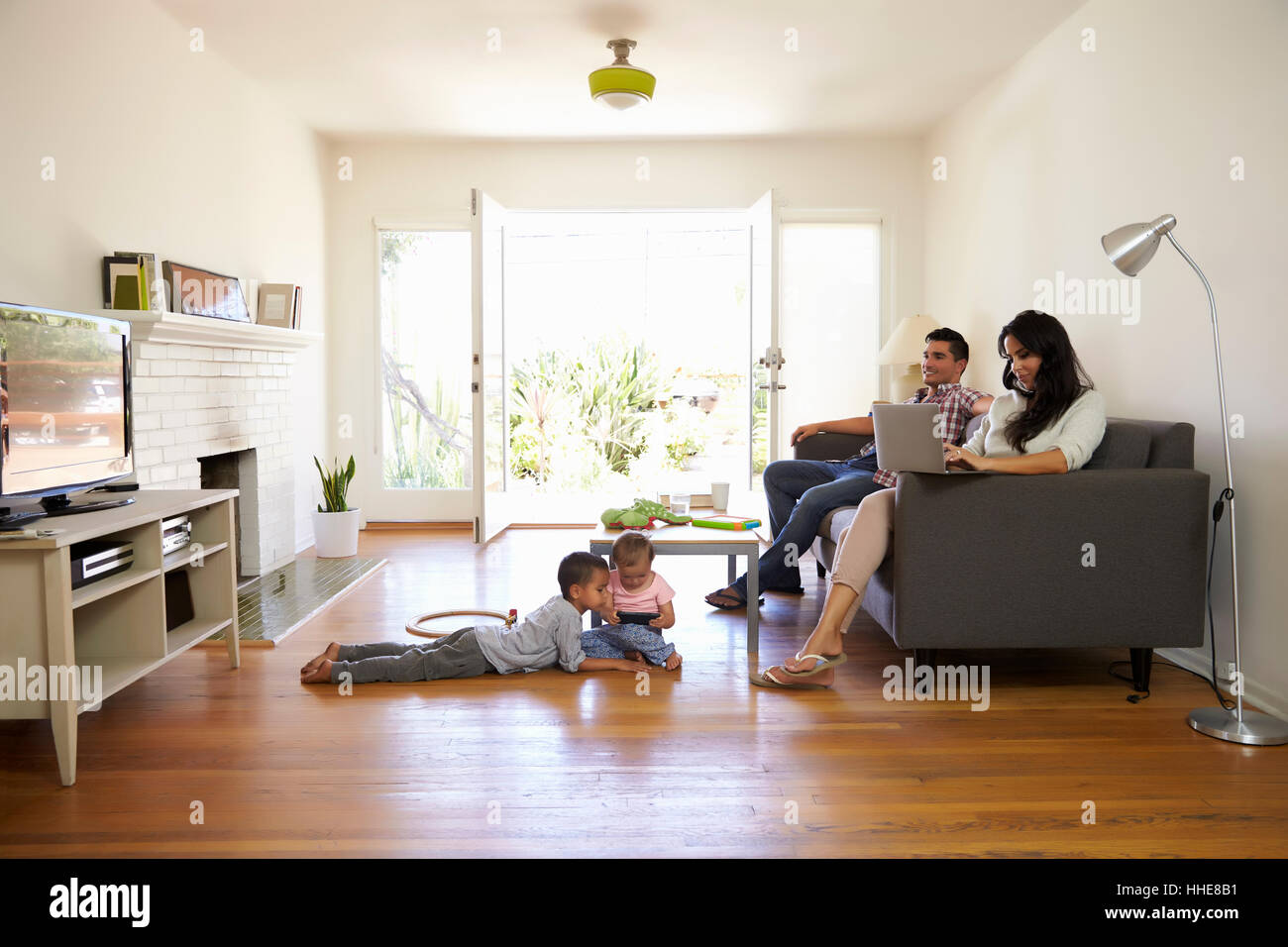 Parents Relax On Sofa As Children Play With Digital Device Stock Photo ...