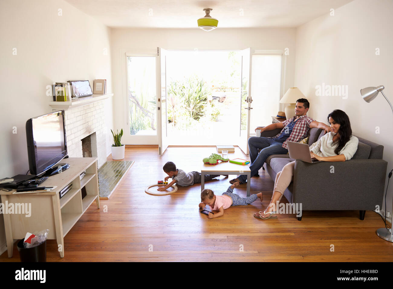 Parents Relax On Sofa As Children Play With Digital Device Stock Photo ...