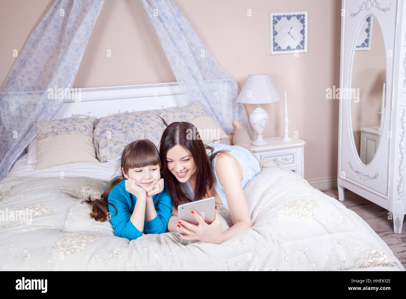 Happy mother and daughter lay in bed with digital tablet, smiling and ...