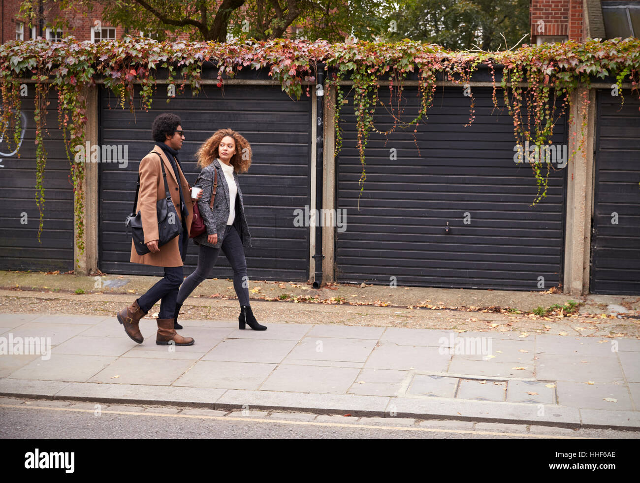 Stylish Young Couple Walking Past Garages On City Street Stock Photo ...