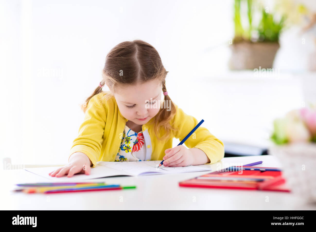 Cute little girl doing homework, reading a book, coloring pages ...