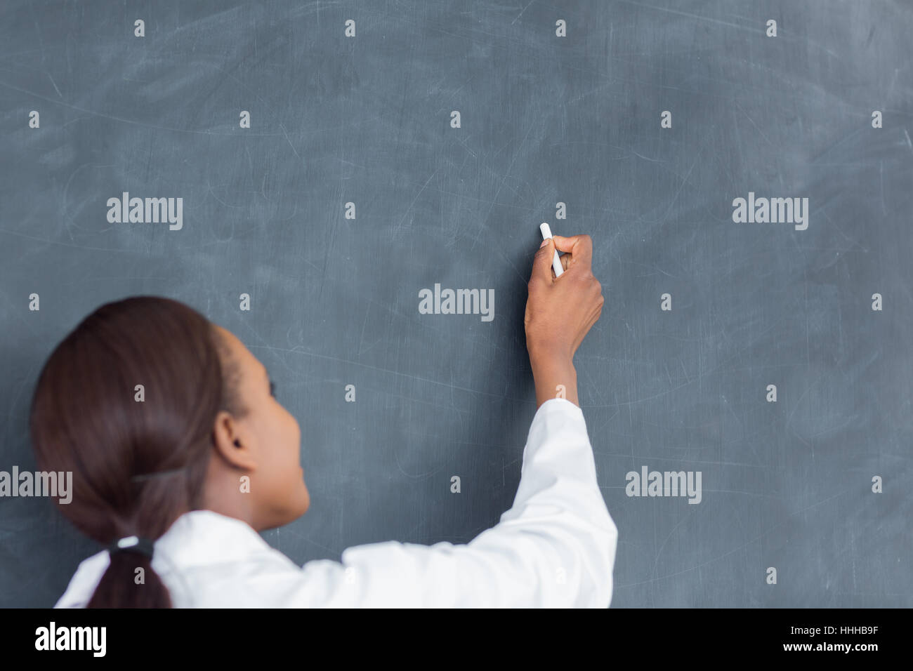 Rear view of a teacher writing on a blackboard in a classroom Stock ...