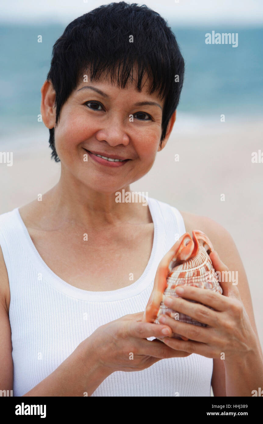 Woman with sea shell at the beach, smiling at camera Stock Photo - Alamy