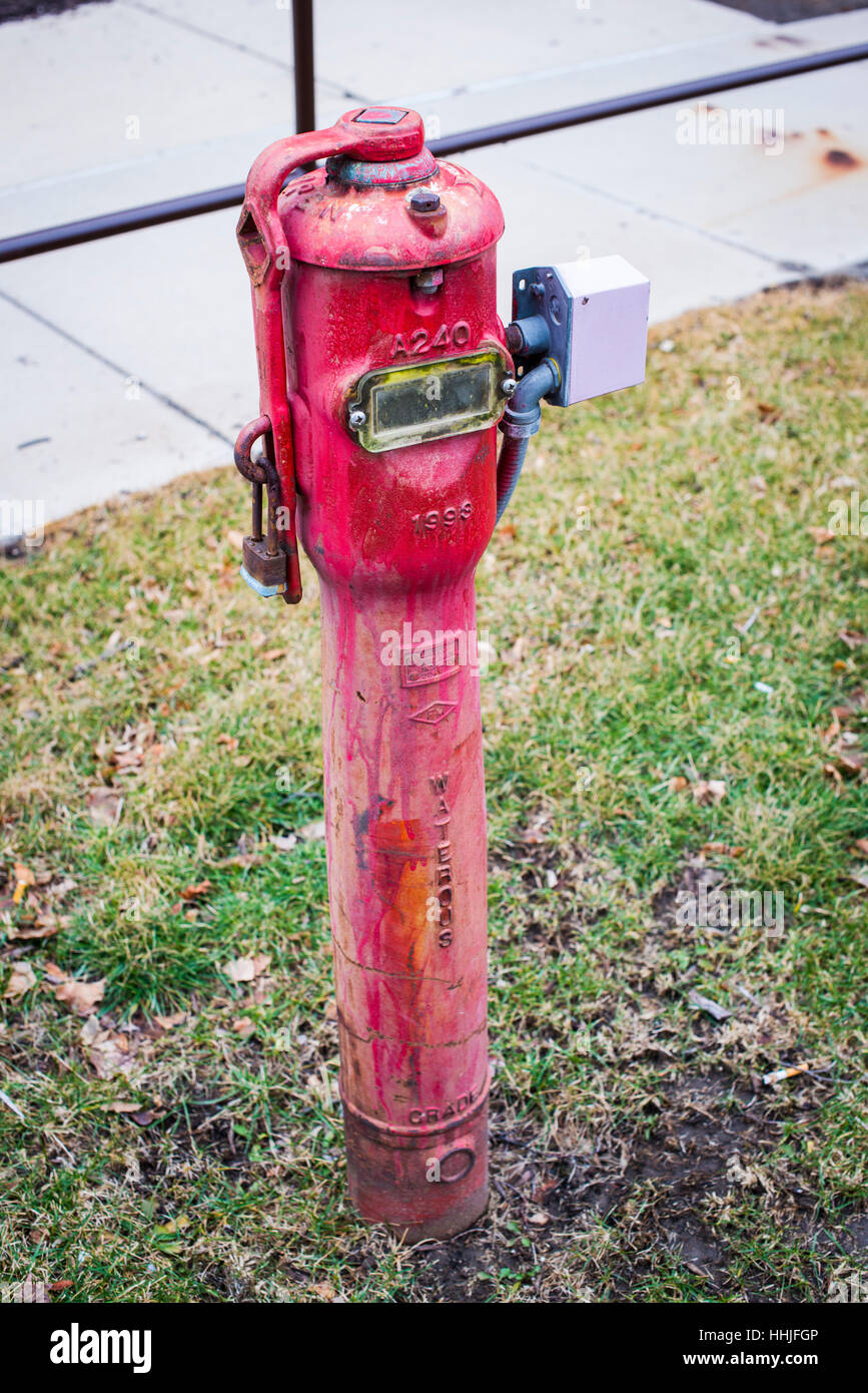An old bright red utility meter near a sidewalk showing signs of wear ...