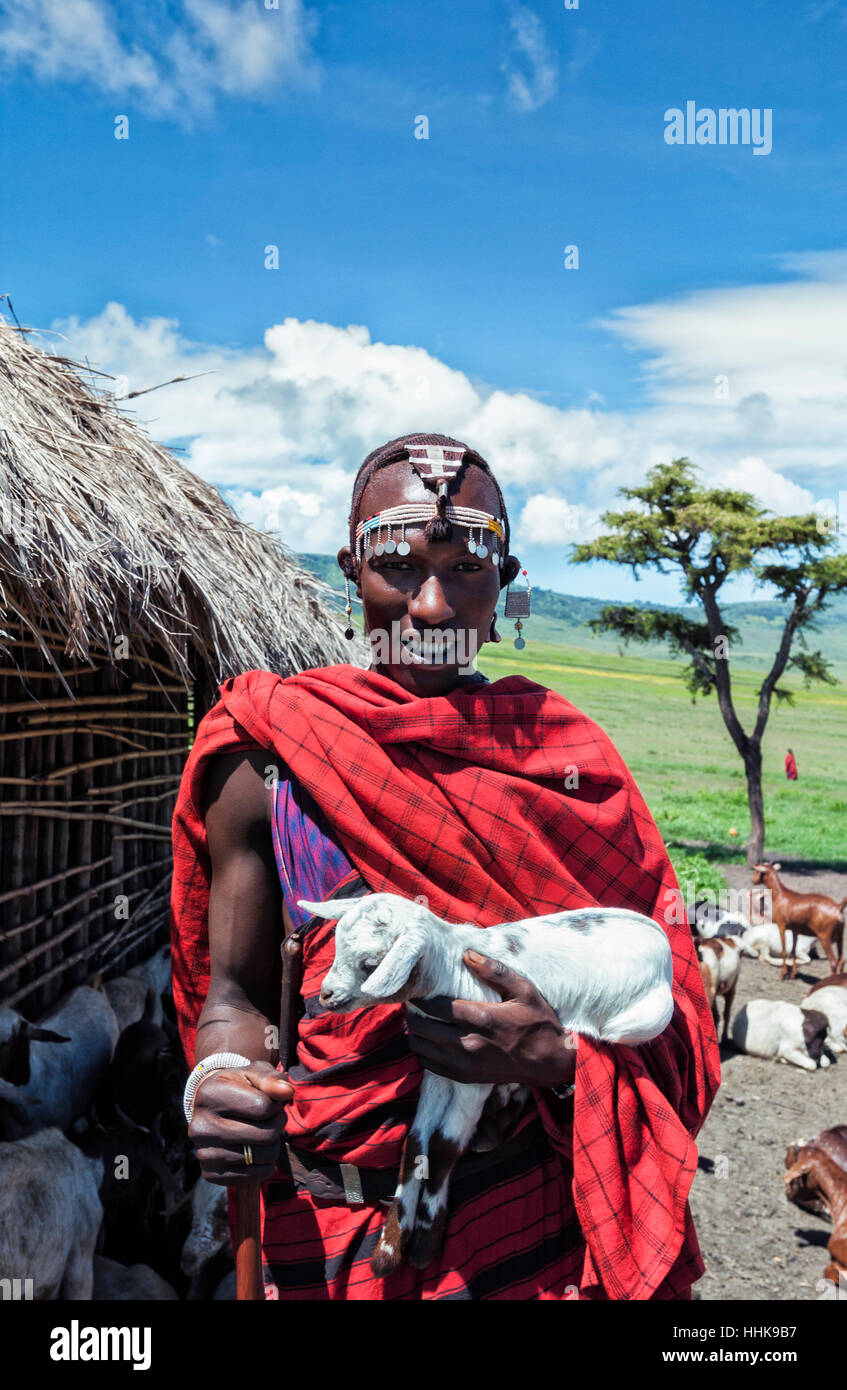 Portrait of an African tribesman carrying a goat in front of his hut in ...