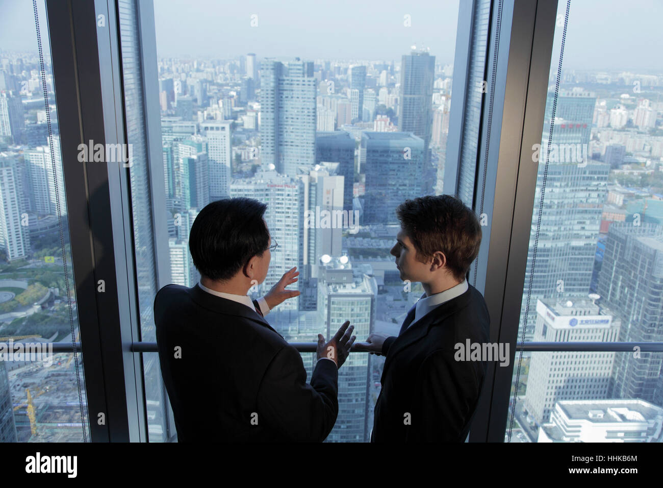 Two men talking in front of window with a view of the city of Beijing ...