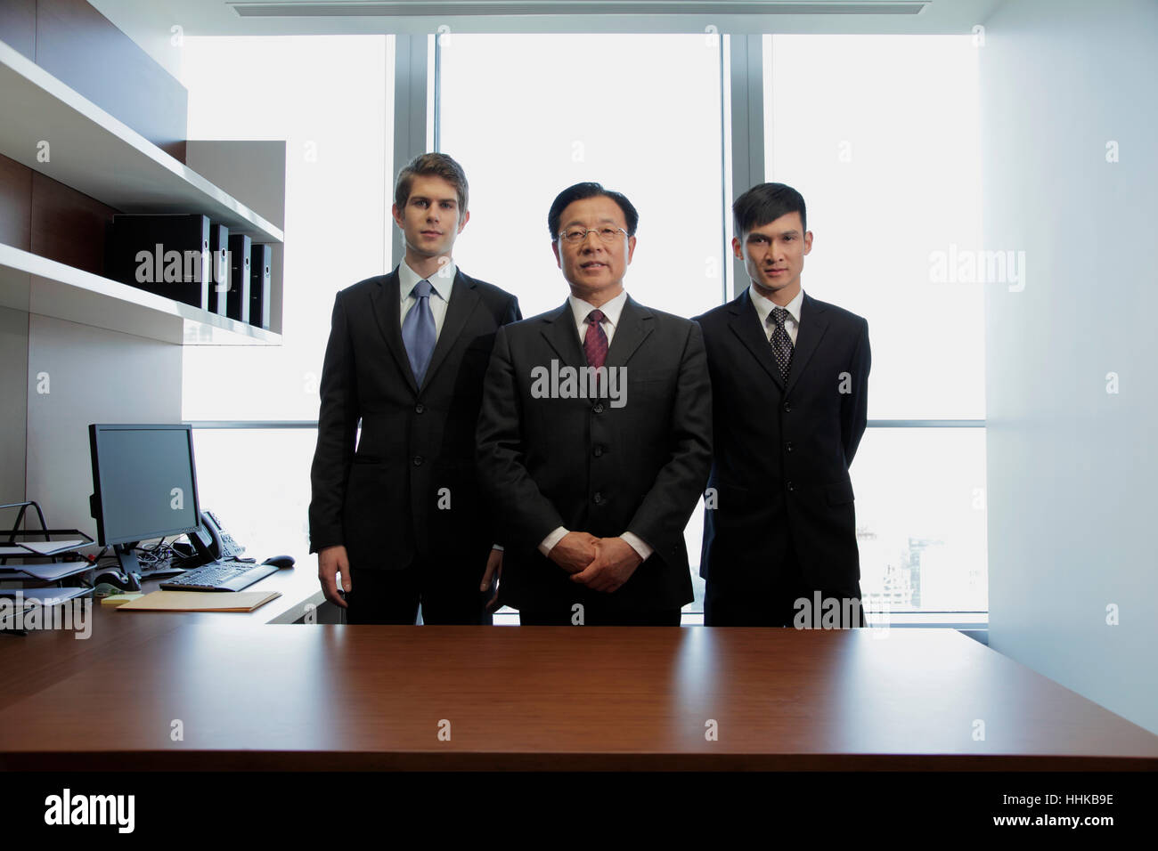 Three business men standing behind a desk Stock Photo - Alamy