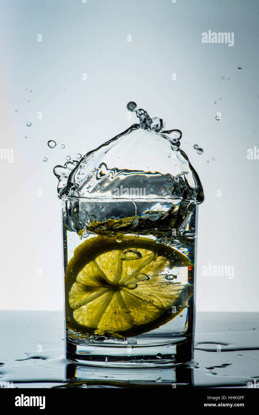 drink and refreshment concept - glass of sparkling water with lemon slices on reflective surface ...