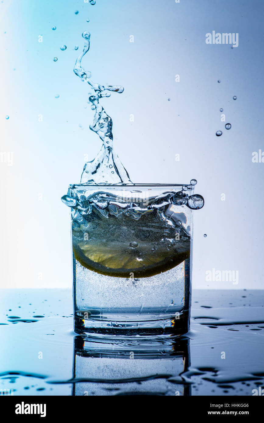 drink and refreshment concept - glass of sparkling water with lemon slices on reflective surface ...