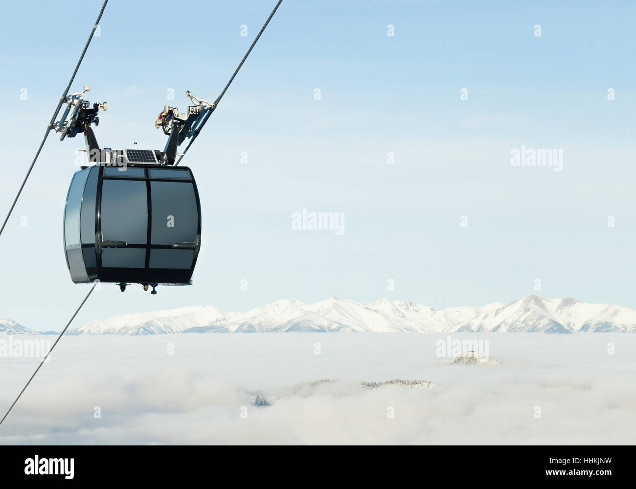Cable car cabin going up above the clouds to the top of a mountain at a ...