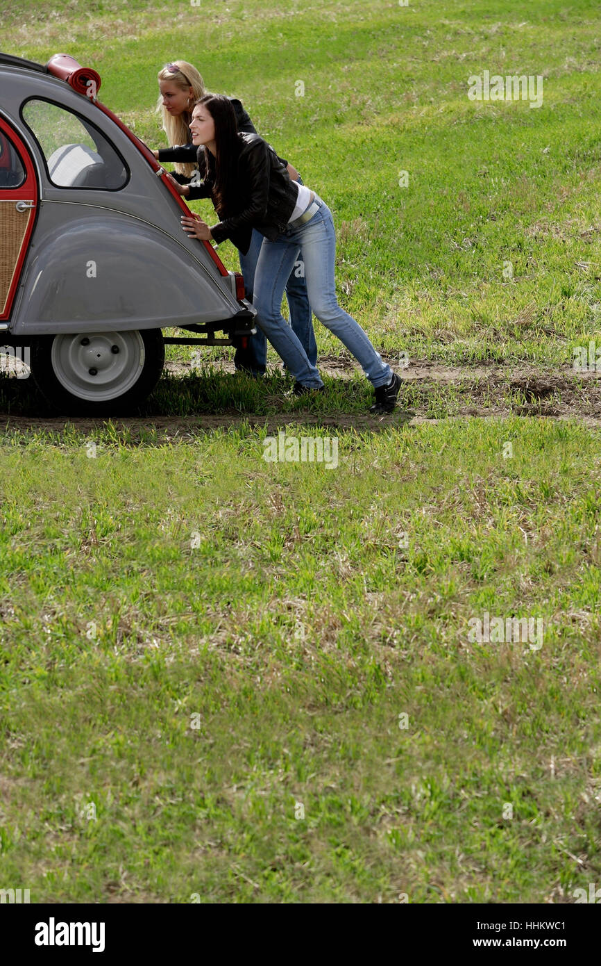 Young women pushing broken down car Stock Photo - Alamy