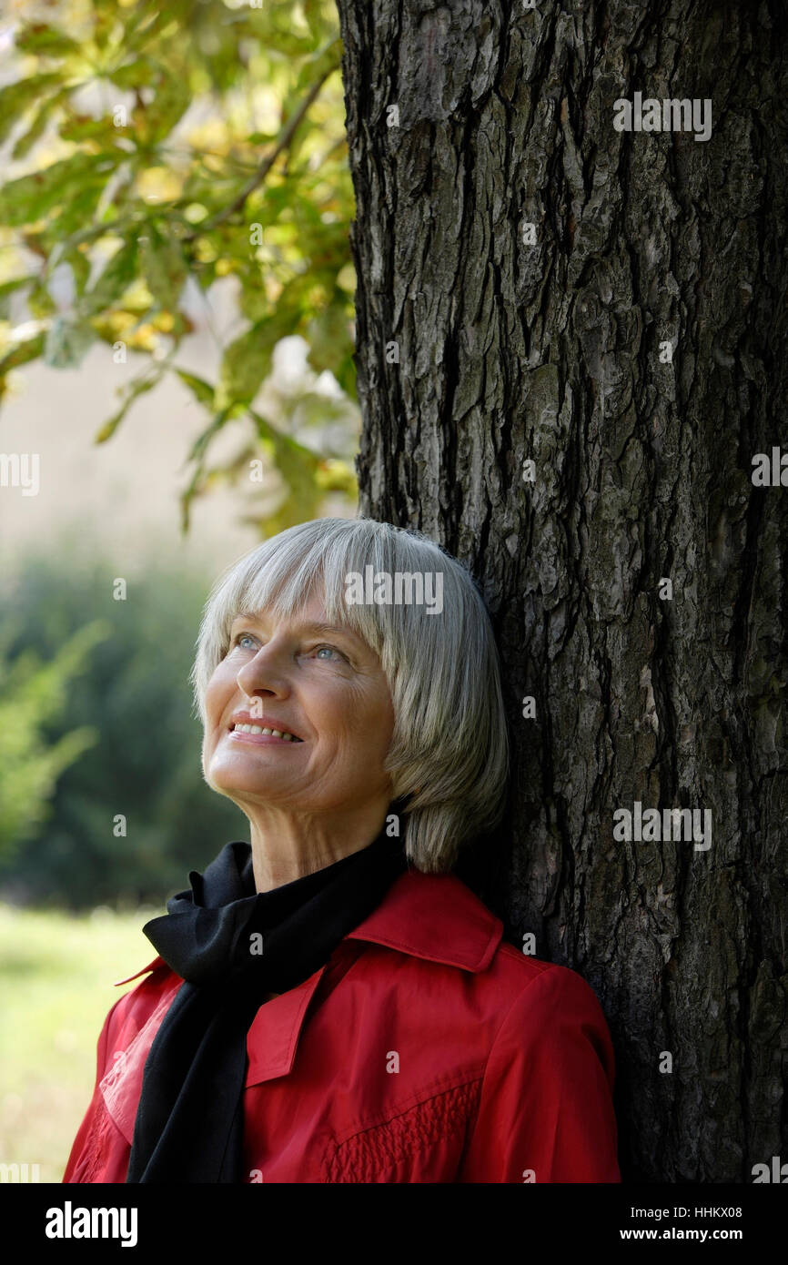 Senior woman leaning against tree Stock Photo - Alamy