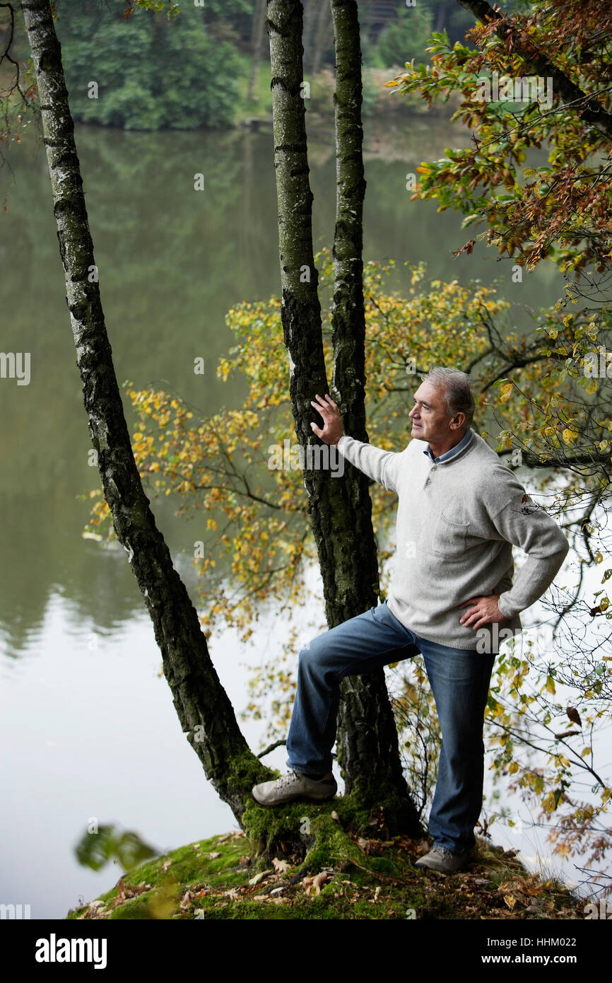 Senior man leaning against tree Stock Photo - Alamy