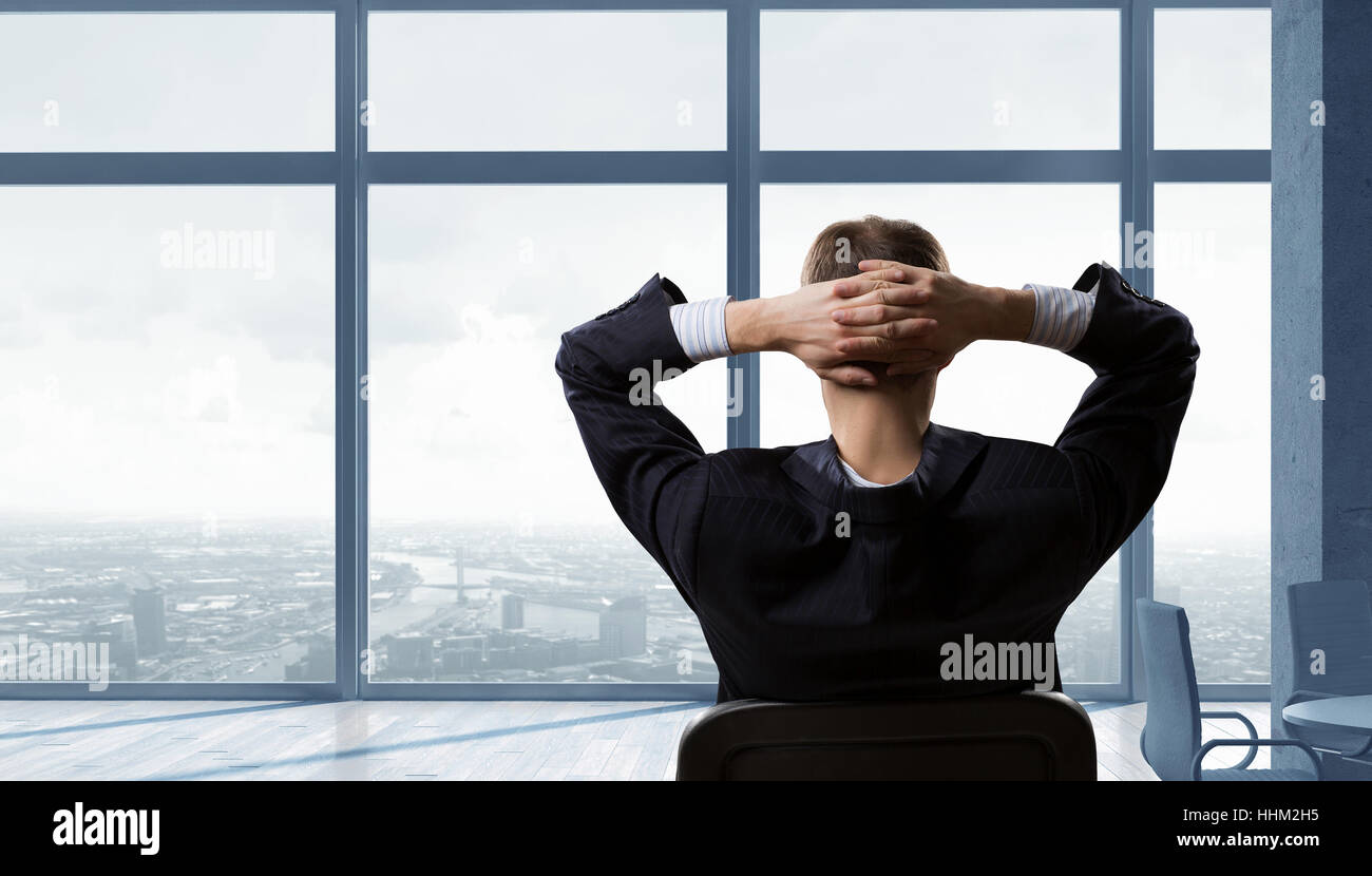 Back view of relaxed businessman sitting on chair with hands on nape ...