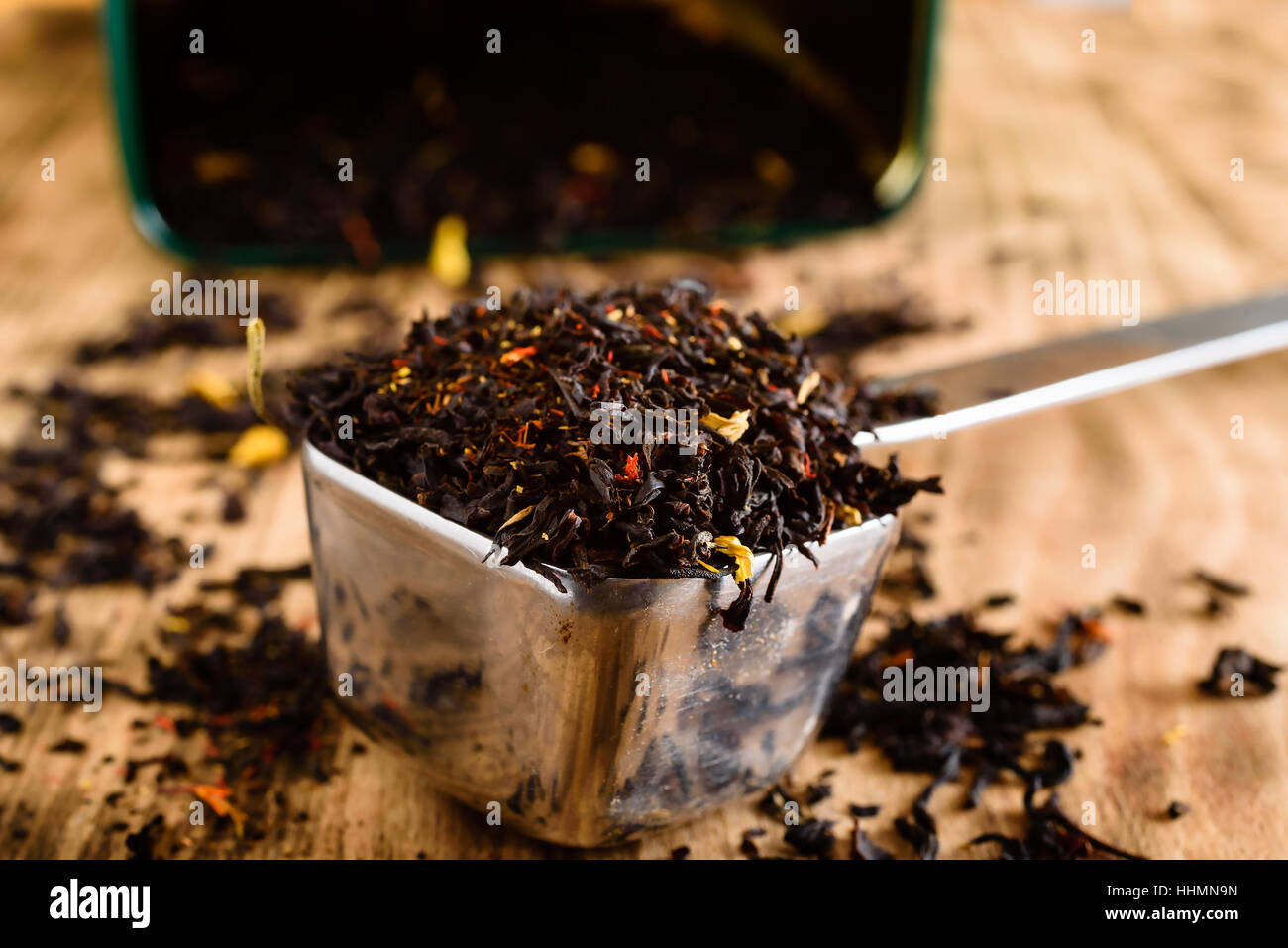 Flavored tea in metal scoop on wooden board. Open tea canister in ...