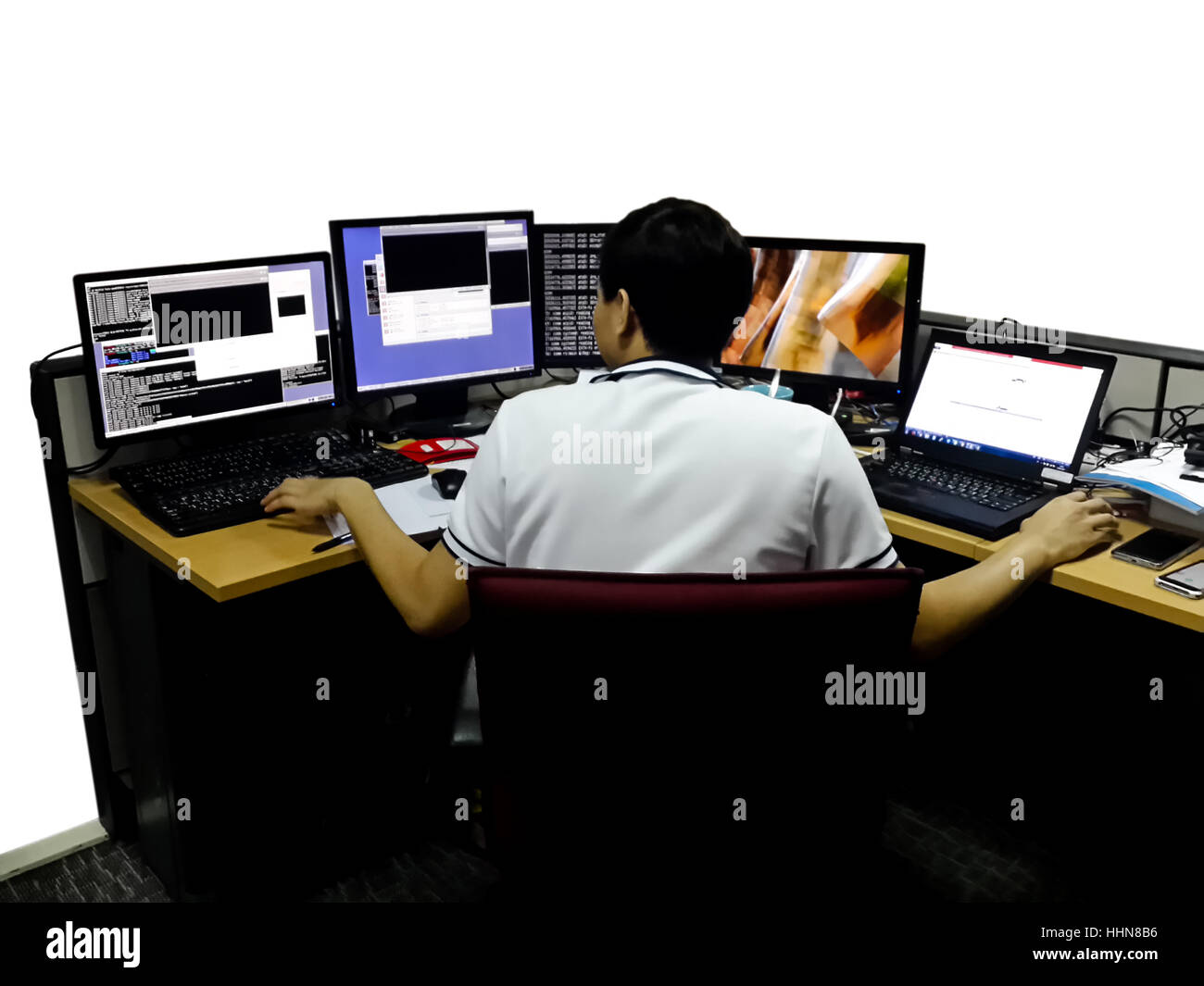 Asian male network engineer working on multiple monitors with one hand ...