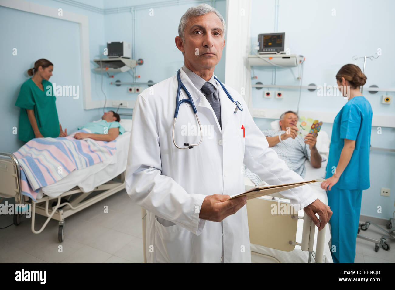 Doctor with clipboard in busy hospital room with two nurses talking to ...