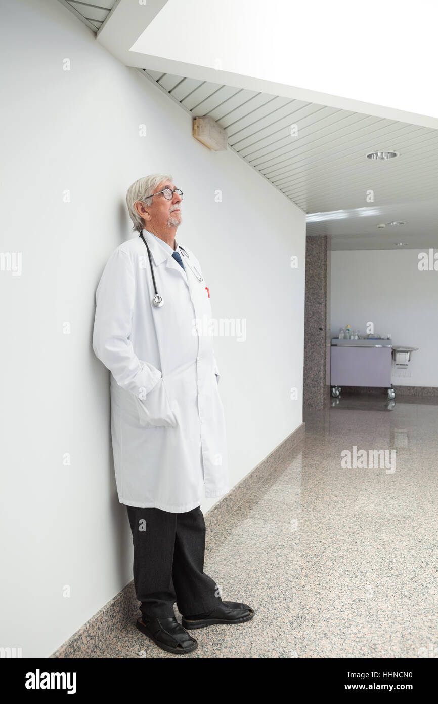Doctor leaning against white wall in hospital corridor Stock Photo - Alamy