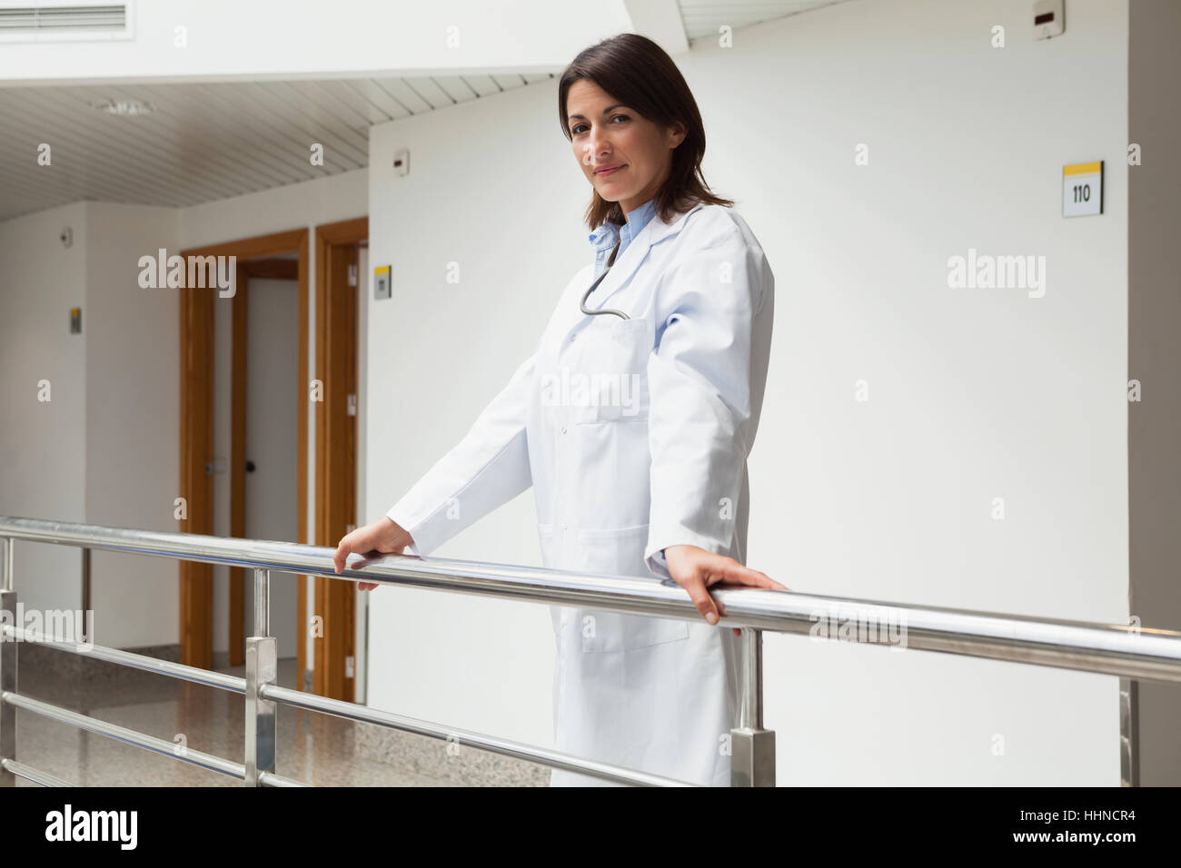 Doctor standing at the railing smiling in hospital corridor Stock Photo ...