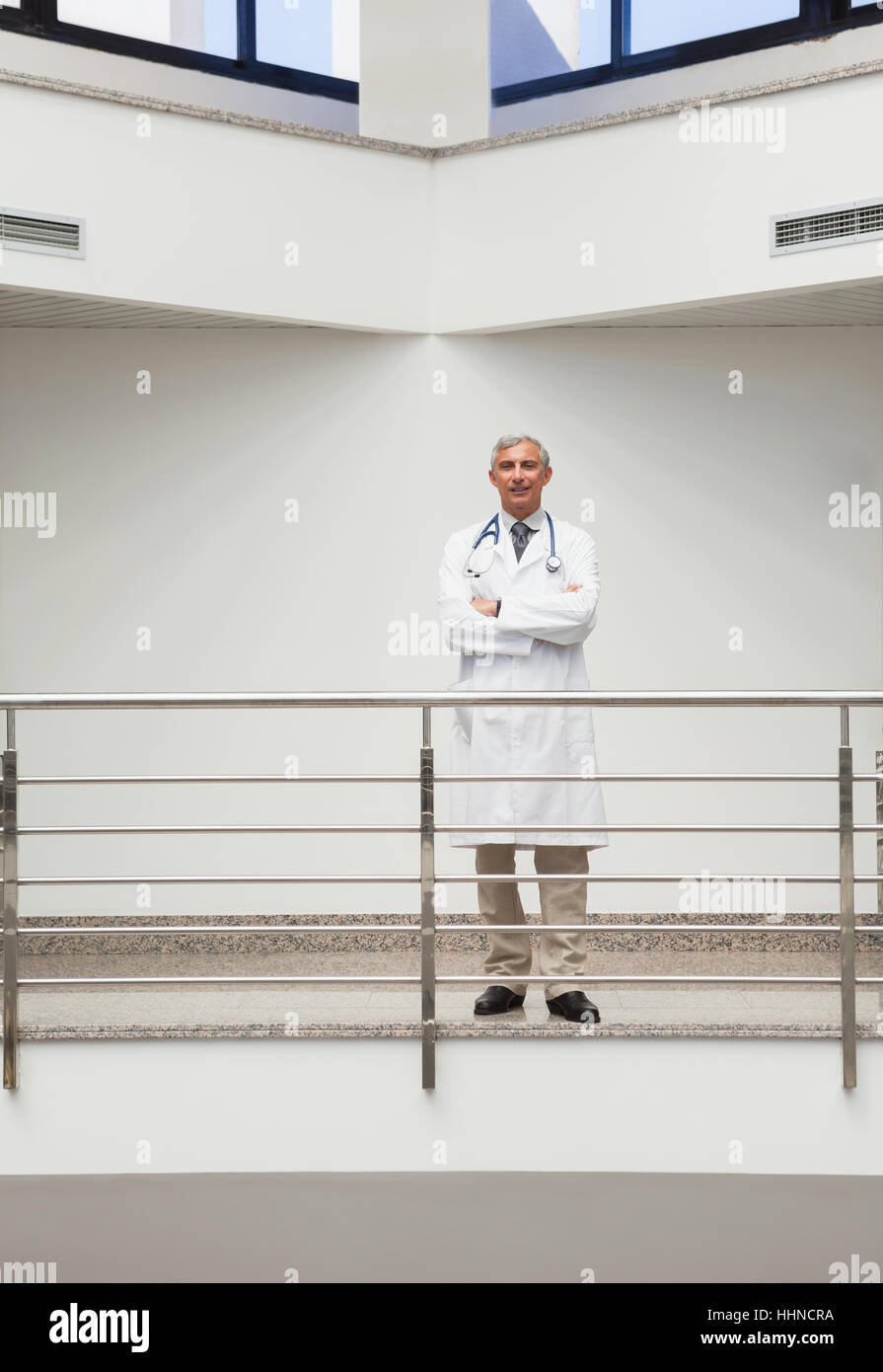 Doctor smiling an the railing with arms crossed on the corridor of the ...