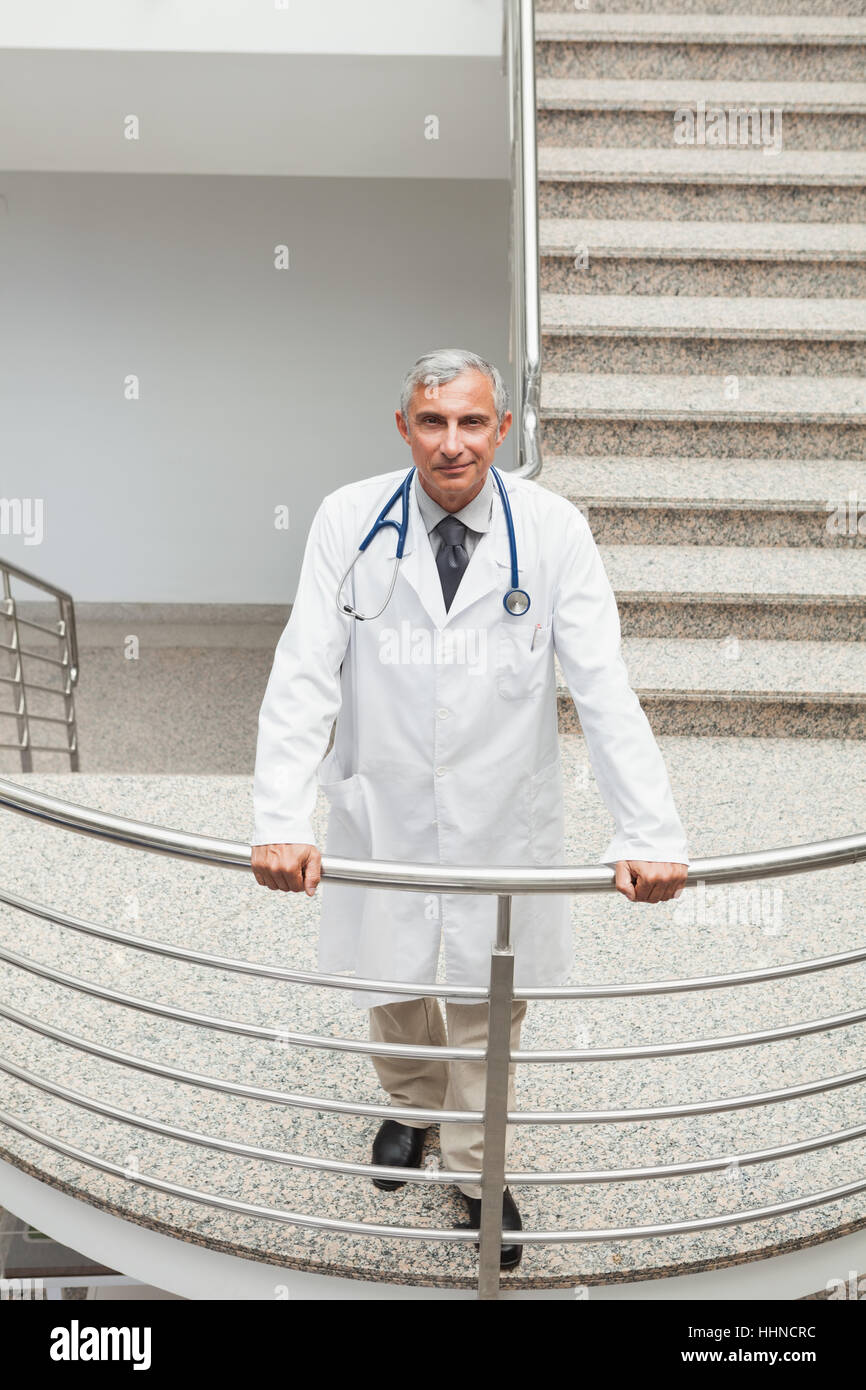 Smiling doctor leaning on the railing of the stairs in the hospital ...
