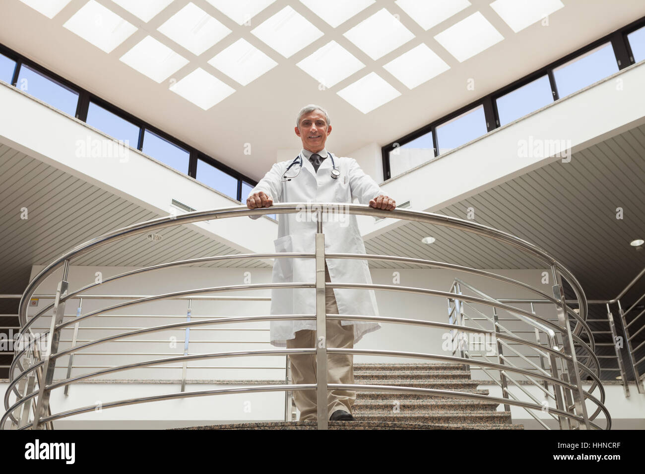 Doctor standing at the railing of the hospital corridor looking down ...