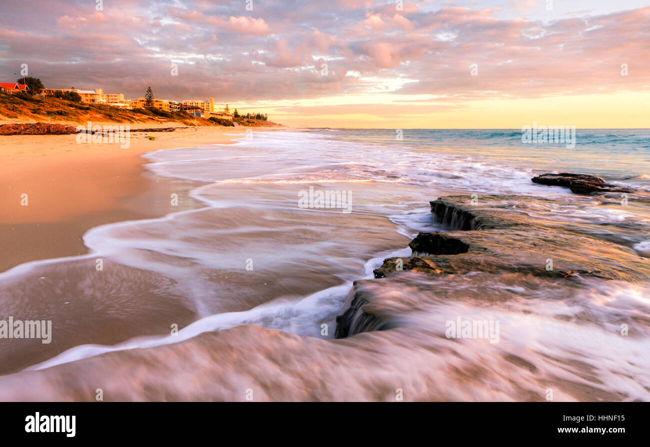 Sunset at North Cottesloe Beach with a wave rolling over a limestone ...