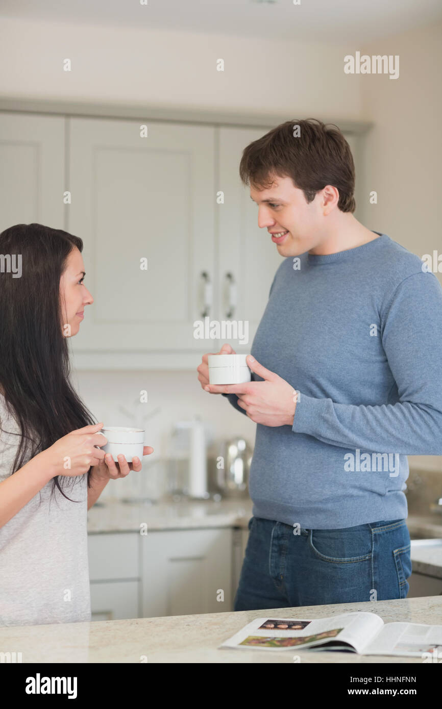 Two people standing in the kitchen and drinking coffee while talking ...