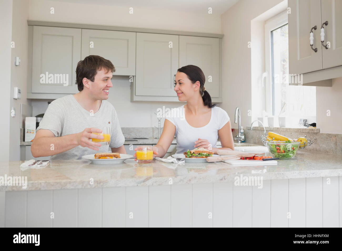 Two people eating sandwiches and drinking juice in the kitchen Stock ...