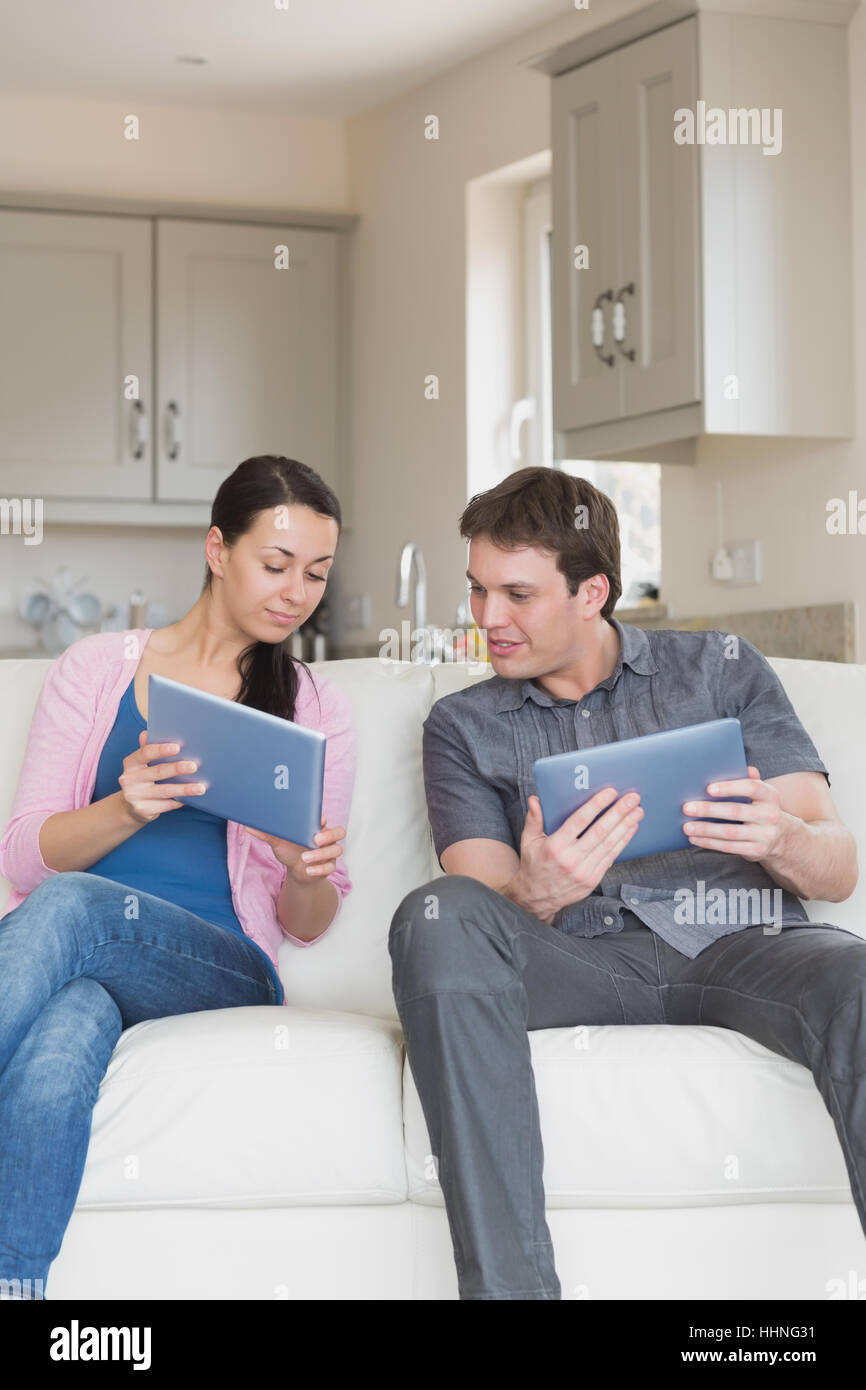 Two friends sitting on the couch and showing how they use the tablet ...
