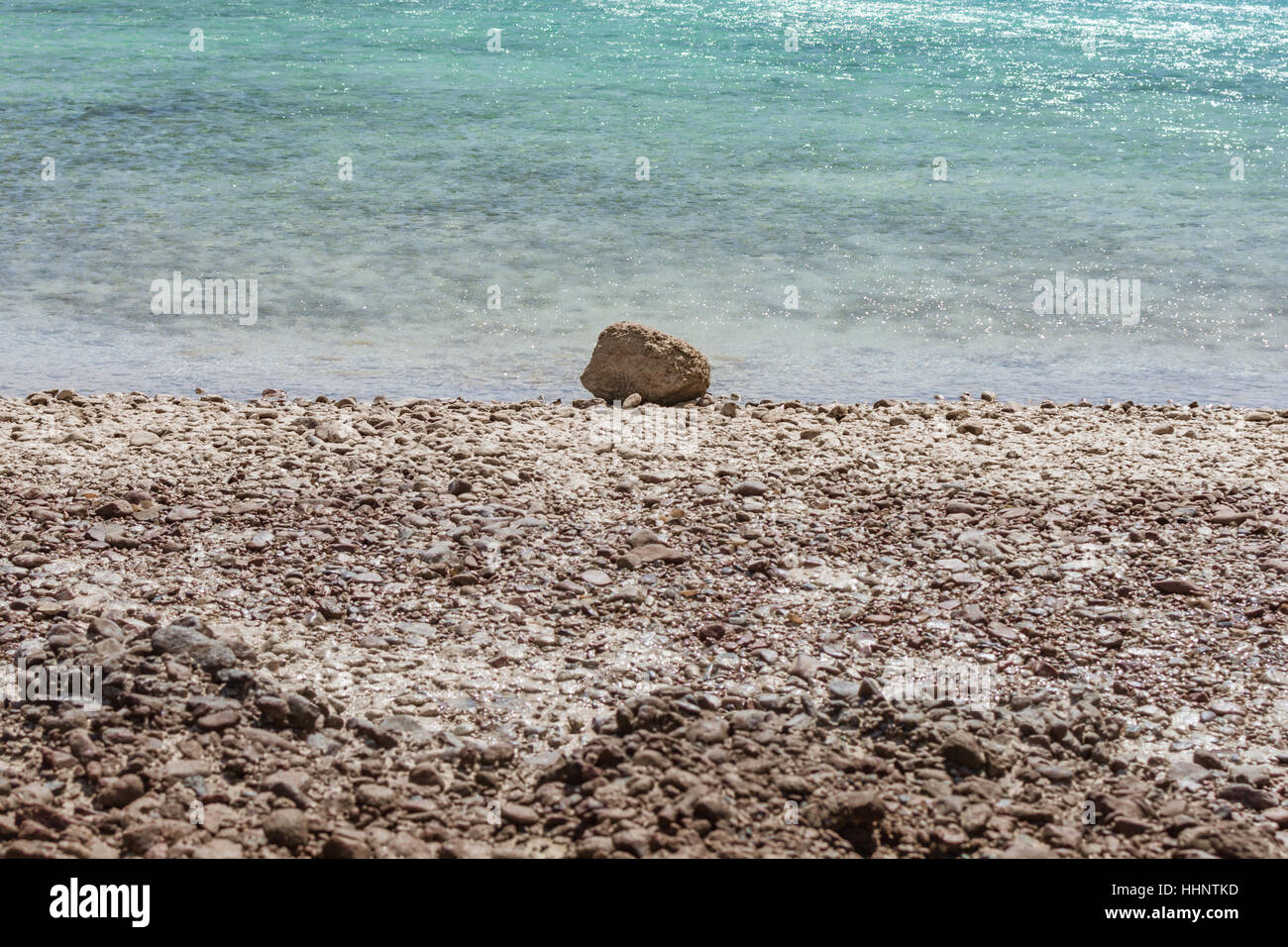 Single rock on crystal clear beach Stock Photo - Alamy