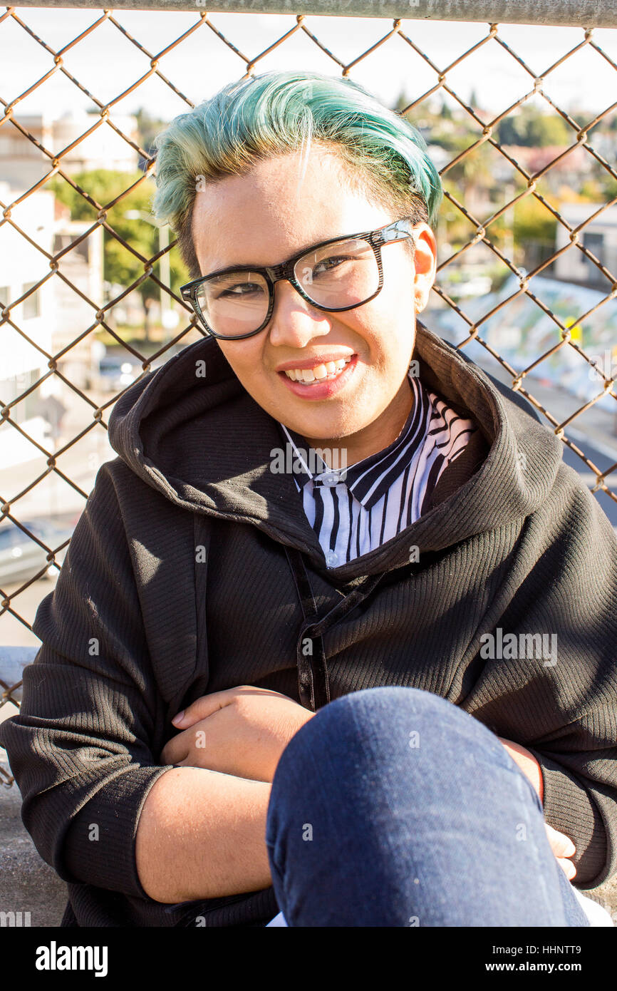 Smiling androgynous Asian woman leaning on chain-link fence Stock Photo ...