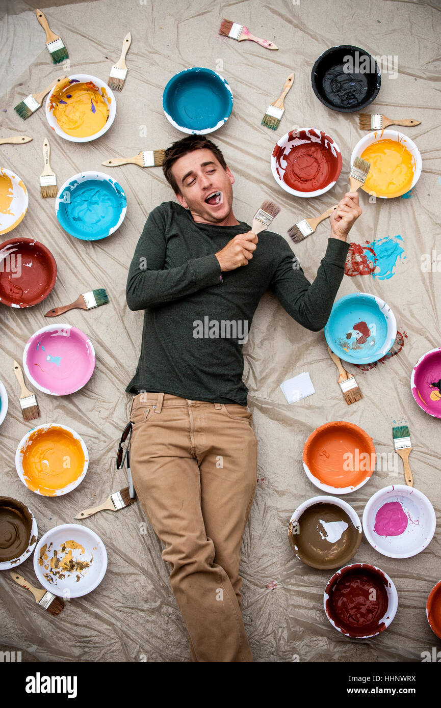 Man laying on tarp holding paintbrushes and singing Stock Photo - Alamy