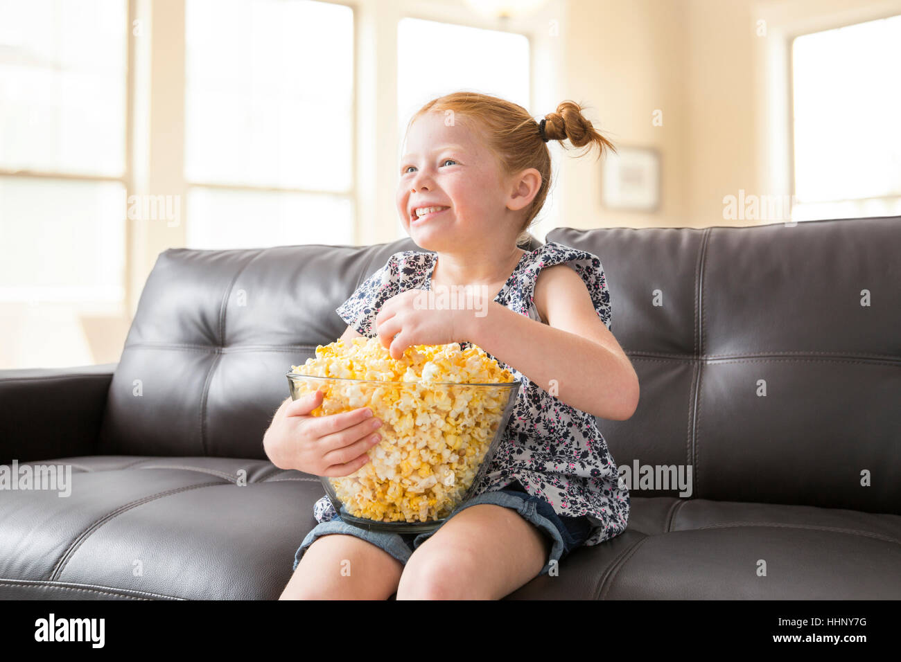 Caucasian girl sitting on sofa eating bowl of popcorn Stock Photo - Alamy
