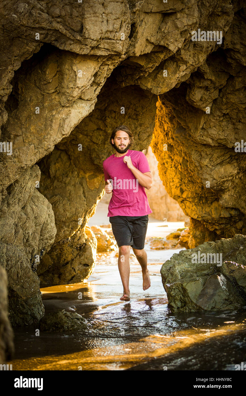 Caucasian man running under rock formation at beach Stock Photo - Alamy