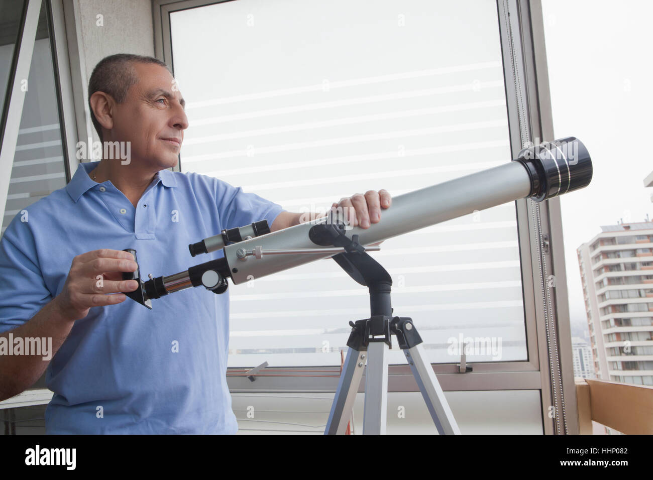 Hispanic man holding telescope near window Stock Photo - Alamy